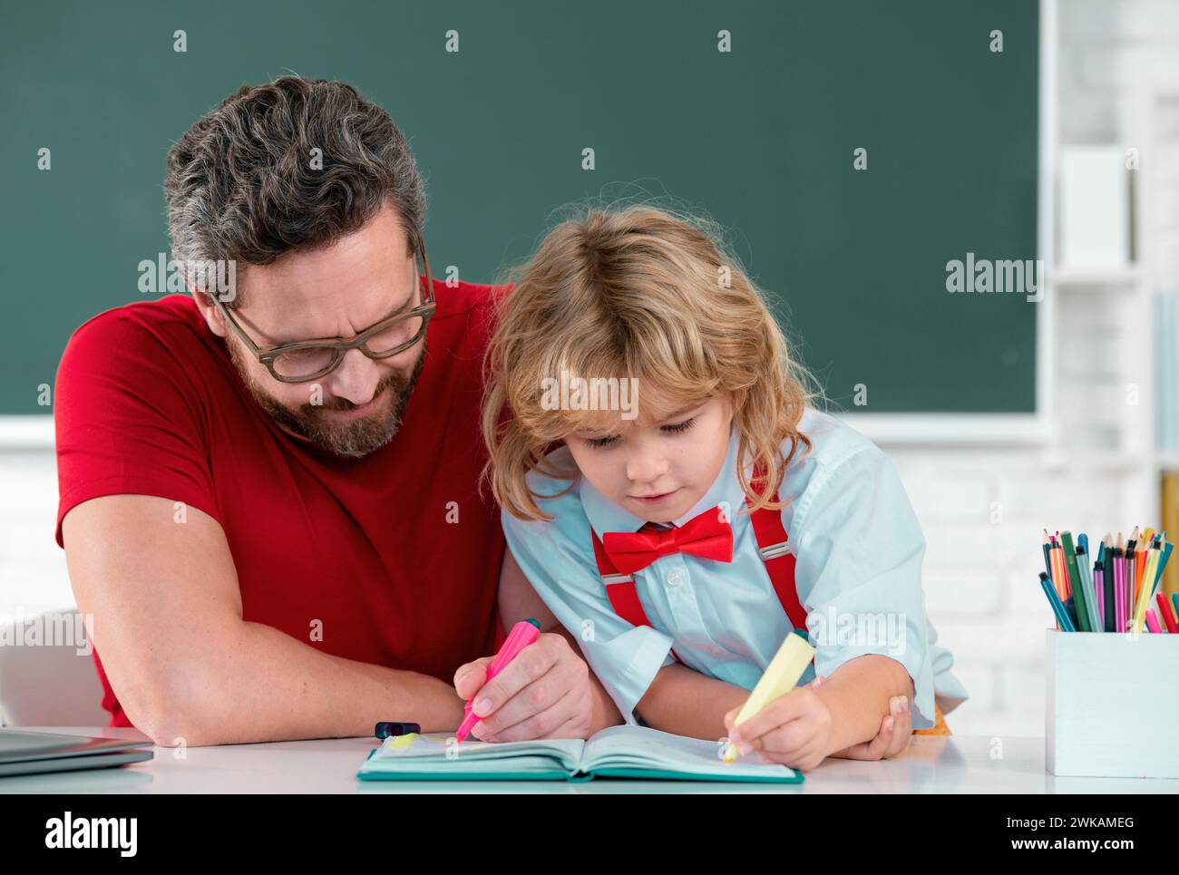 Teacher helping child student pupil from elementary school in classroom ...