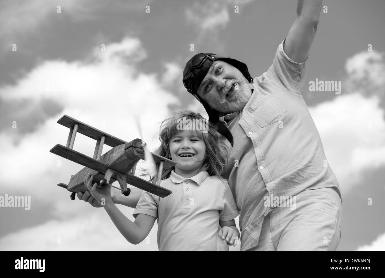 Funny grandson child and grandfather playing with wooden plane against ...