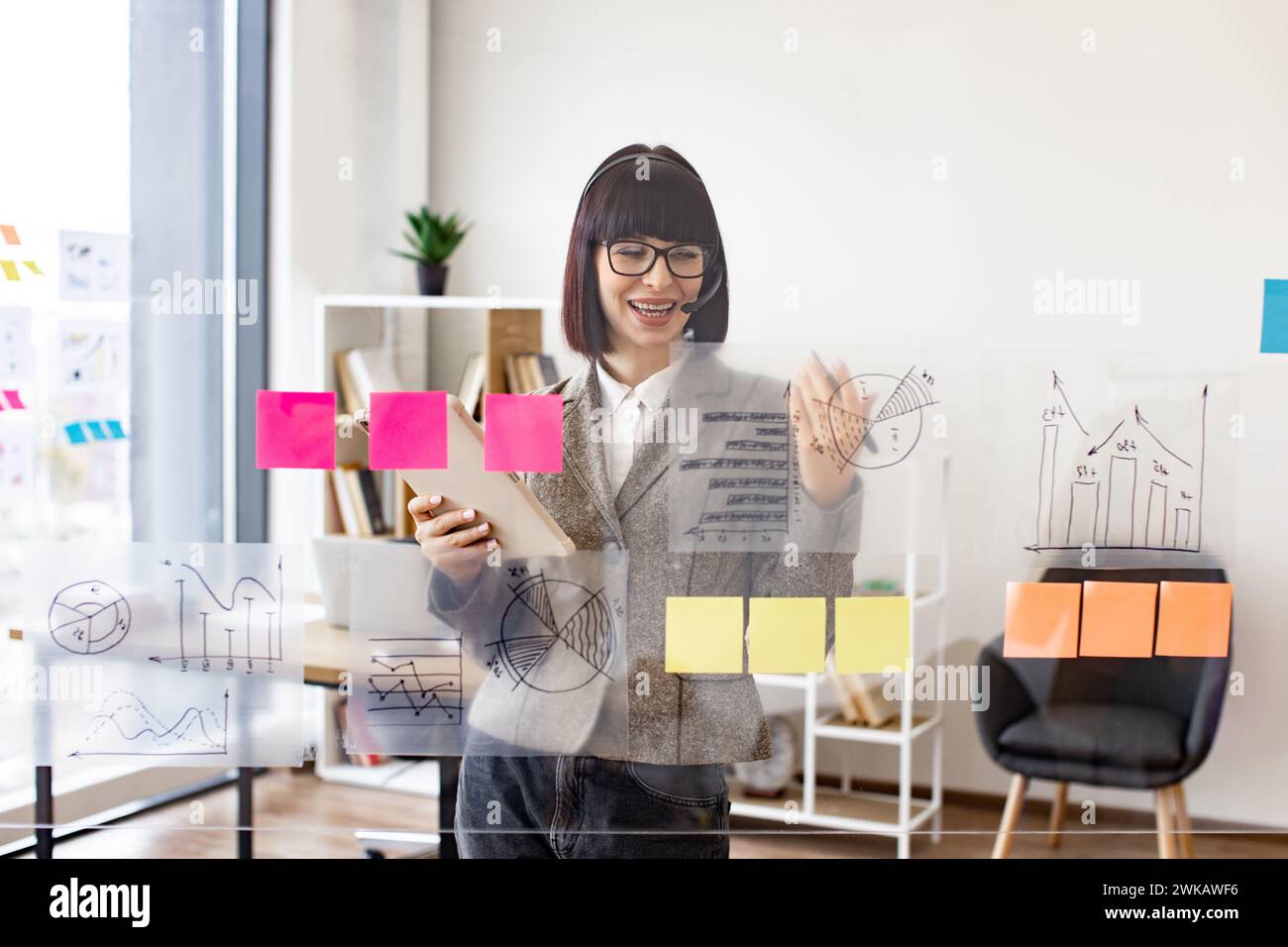 Serious young female worker rewriting notes from tablet in meeting room ...