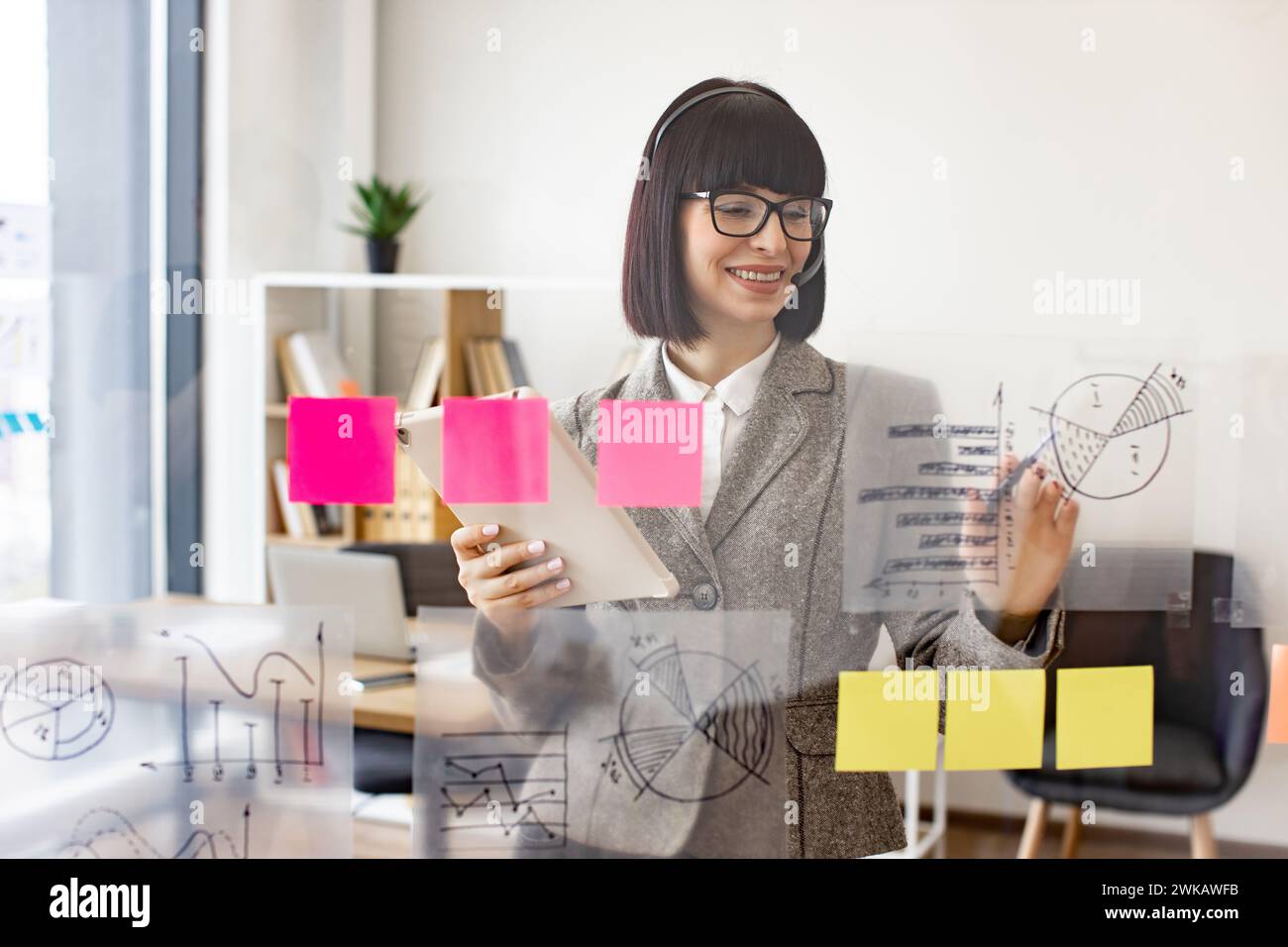 Concentrated caucasian woman in headphones writing on transparent board ...