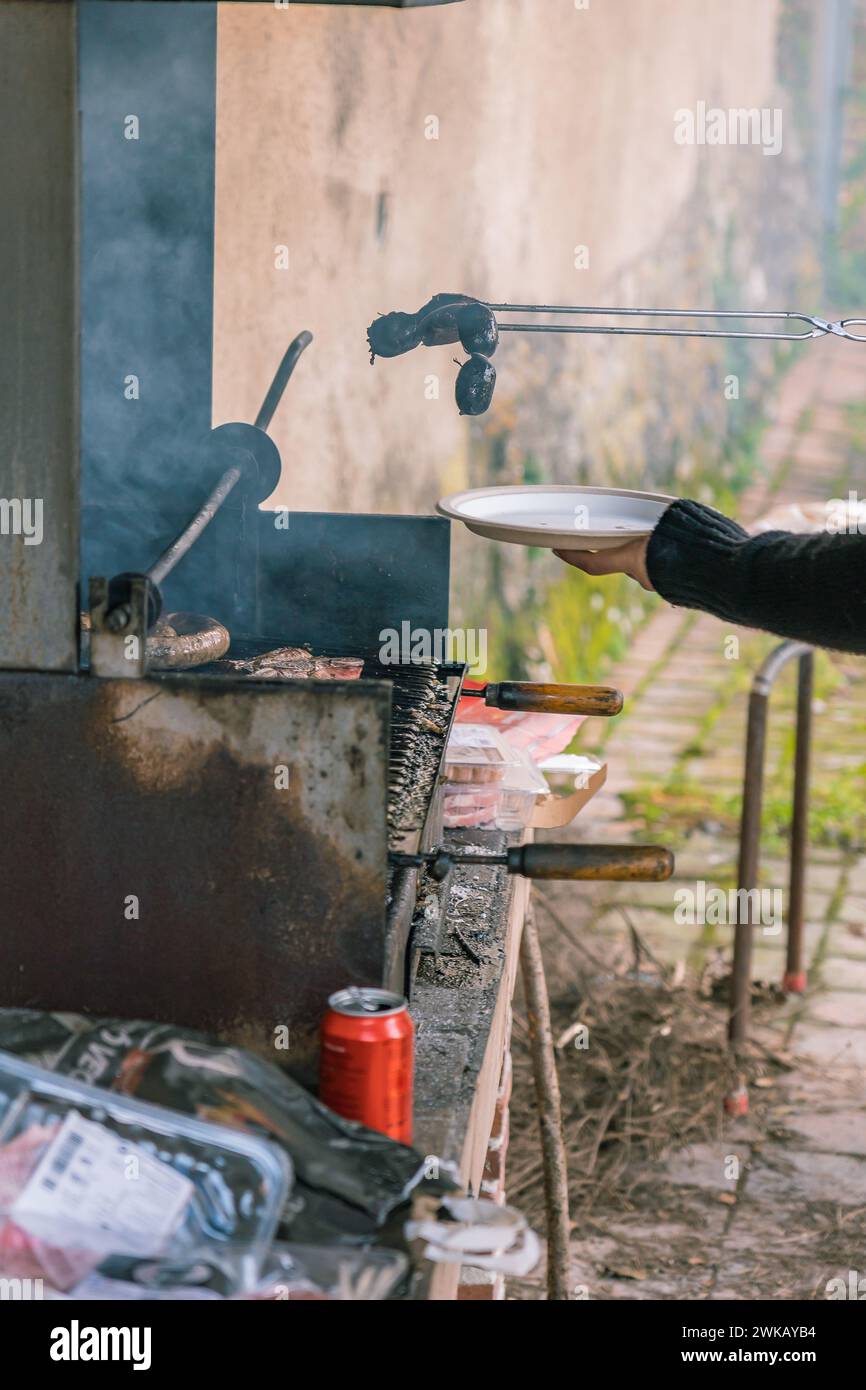 Arm of a white woman removing meat from the barbecue with tongs to put ...
