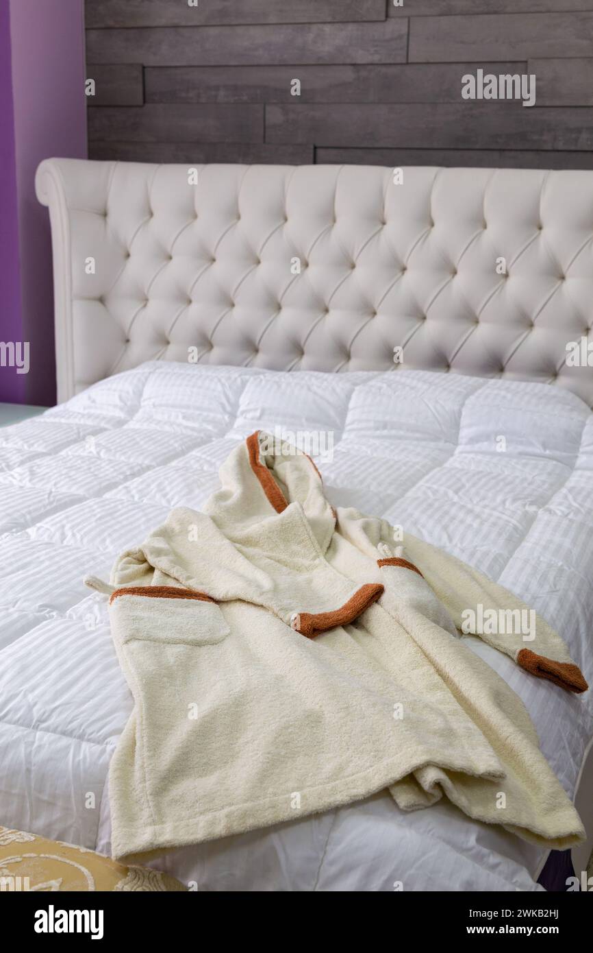 A terry-cloth women's robe of pale yellow color lies on a bed covered ...