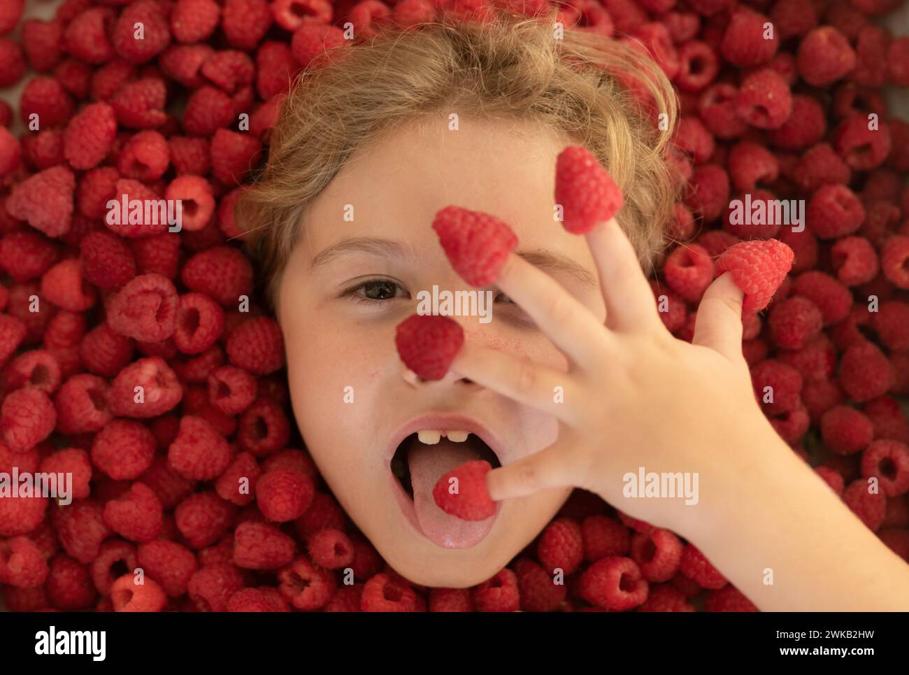 Kid eating raspberries. Top view photo of child face in raspberries ...