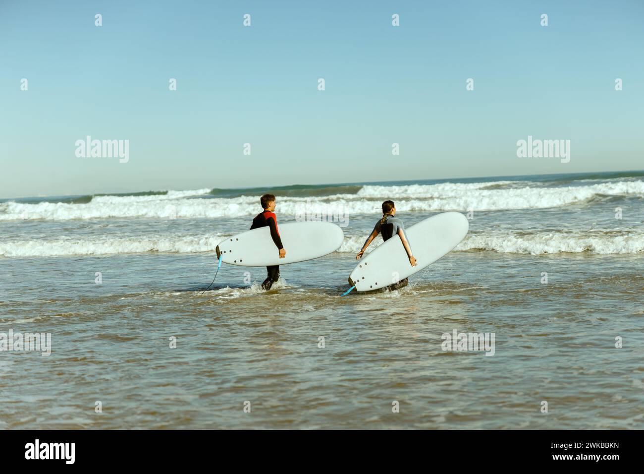 Back view of surfers with surfboards entering towards ocean for surfing ...
