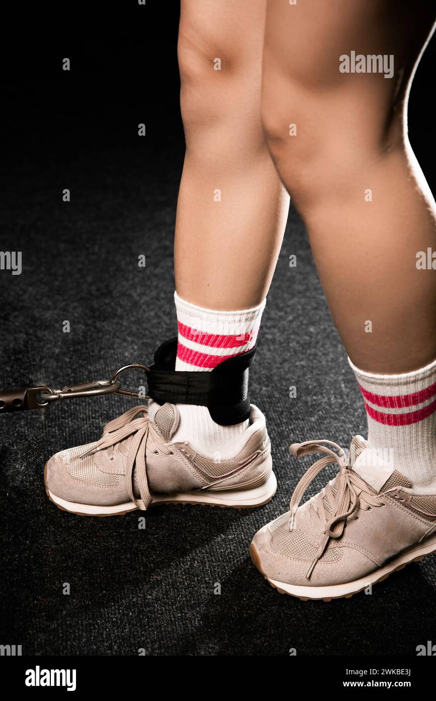 Young woman in trainers buckling a leather strap to her ankle in a gym ...