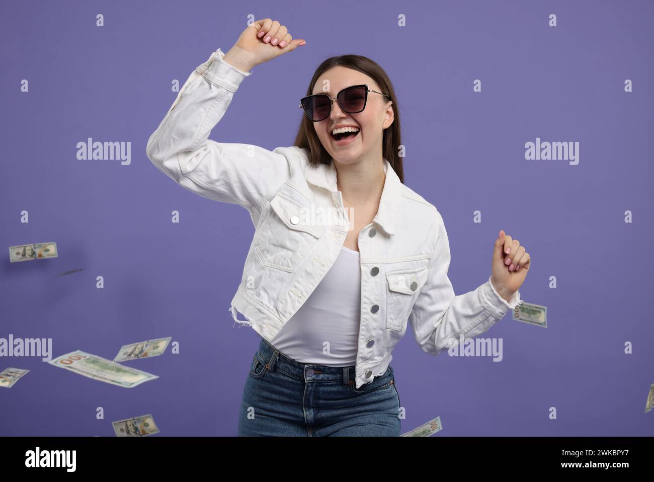 Happy woman under money shower on purple background Stock Photo - Alamy