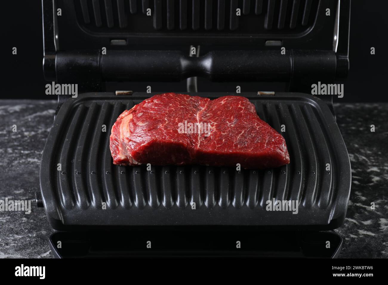 Cooking fresh beef cut on electric grill at black table Stock Photo - Alamy