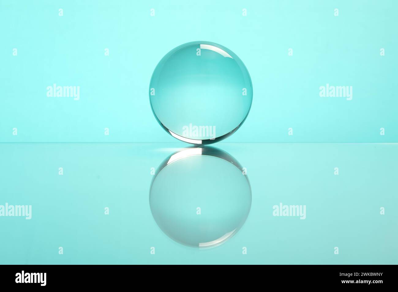 Transparent glass ball on mirror surface against turquoise background ...