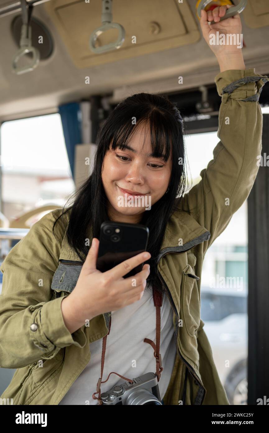A positive Asian female solo traveler using her smartphone while ...