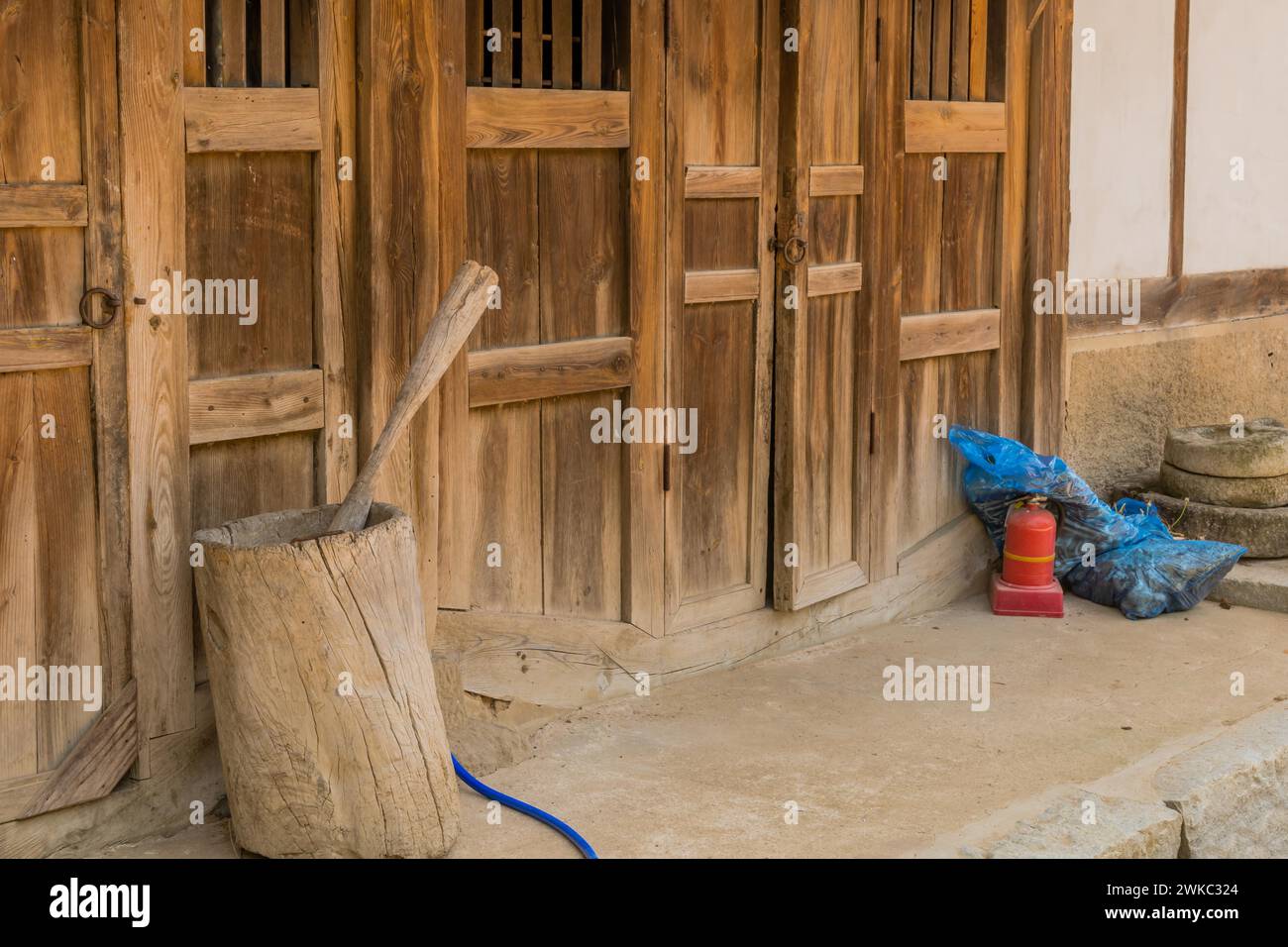 Wooden hand grain pulverizer in front of wooden building in public park ...