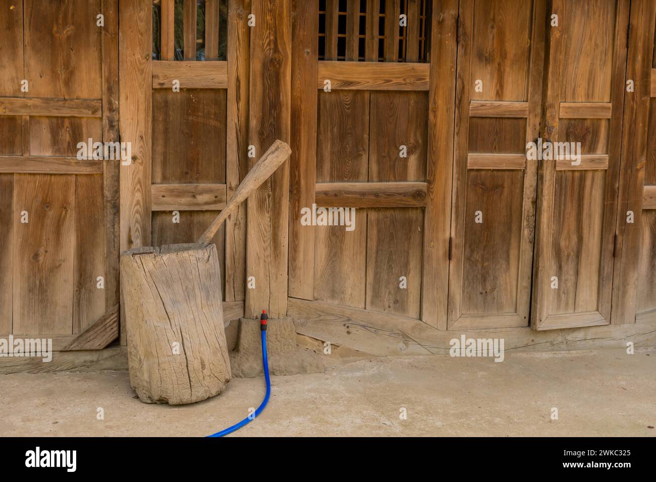 Wooden hand grain pulverizer in front of wooden building in public park ...