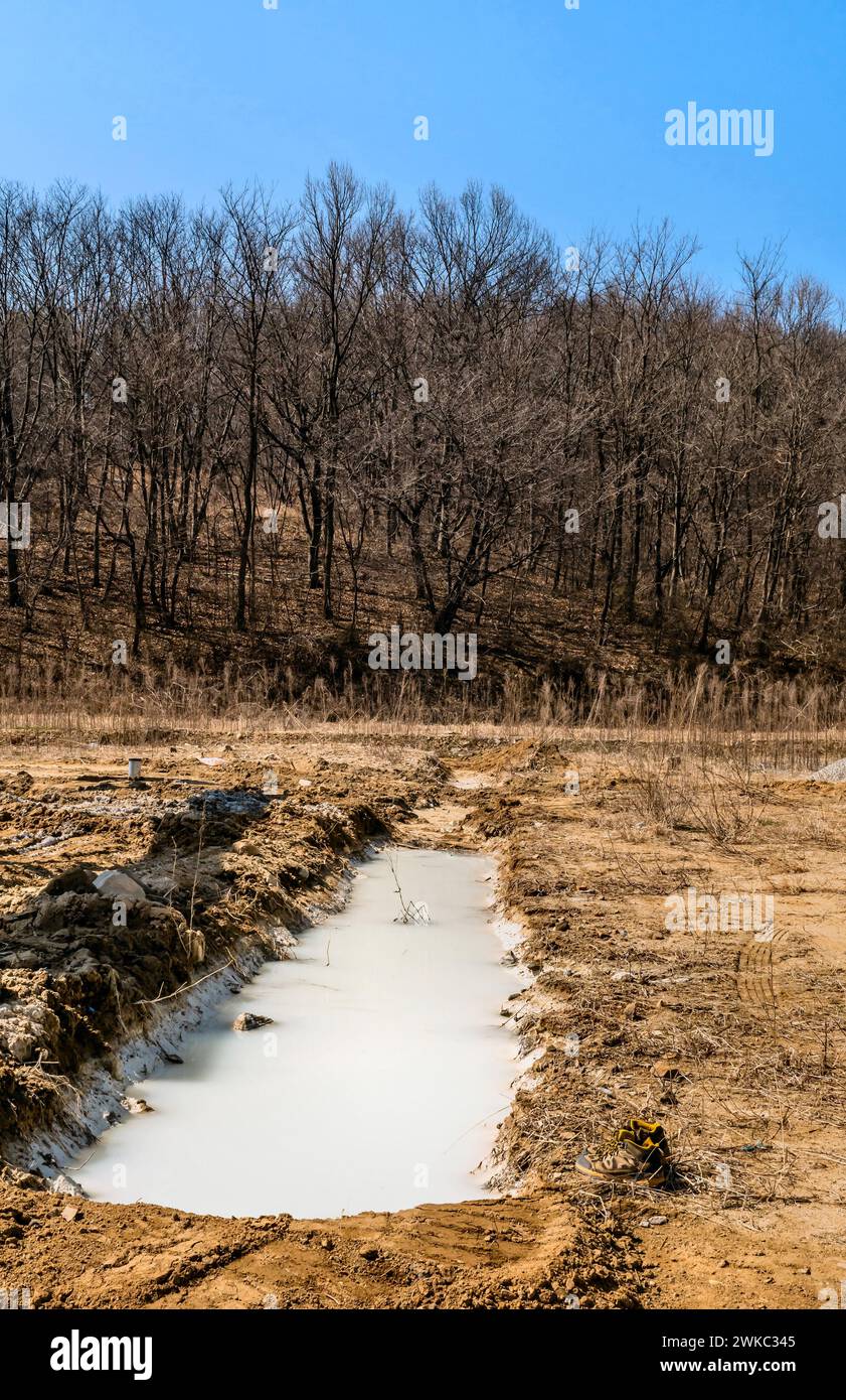 Hiking shoes left beside man made ditch filled with milky water in ...