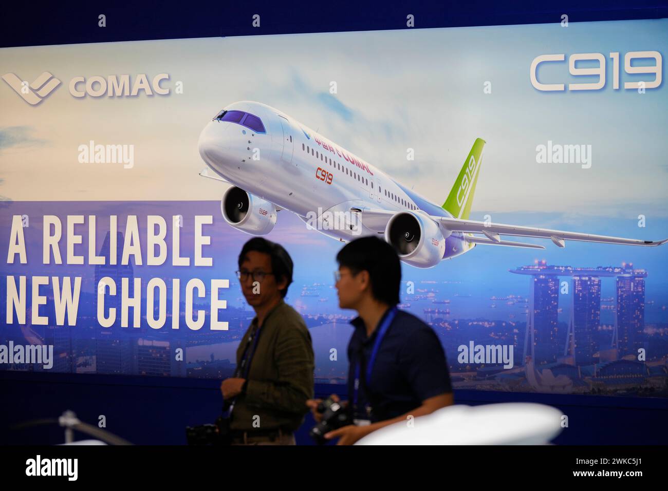 Visitors walk in front of a poster of China's Comac C919 aircraft ...