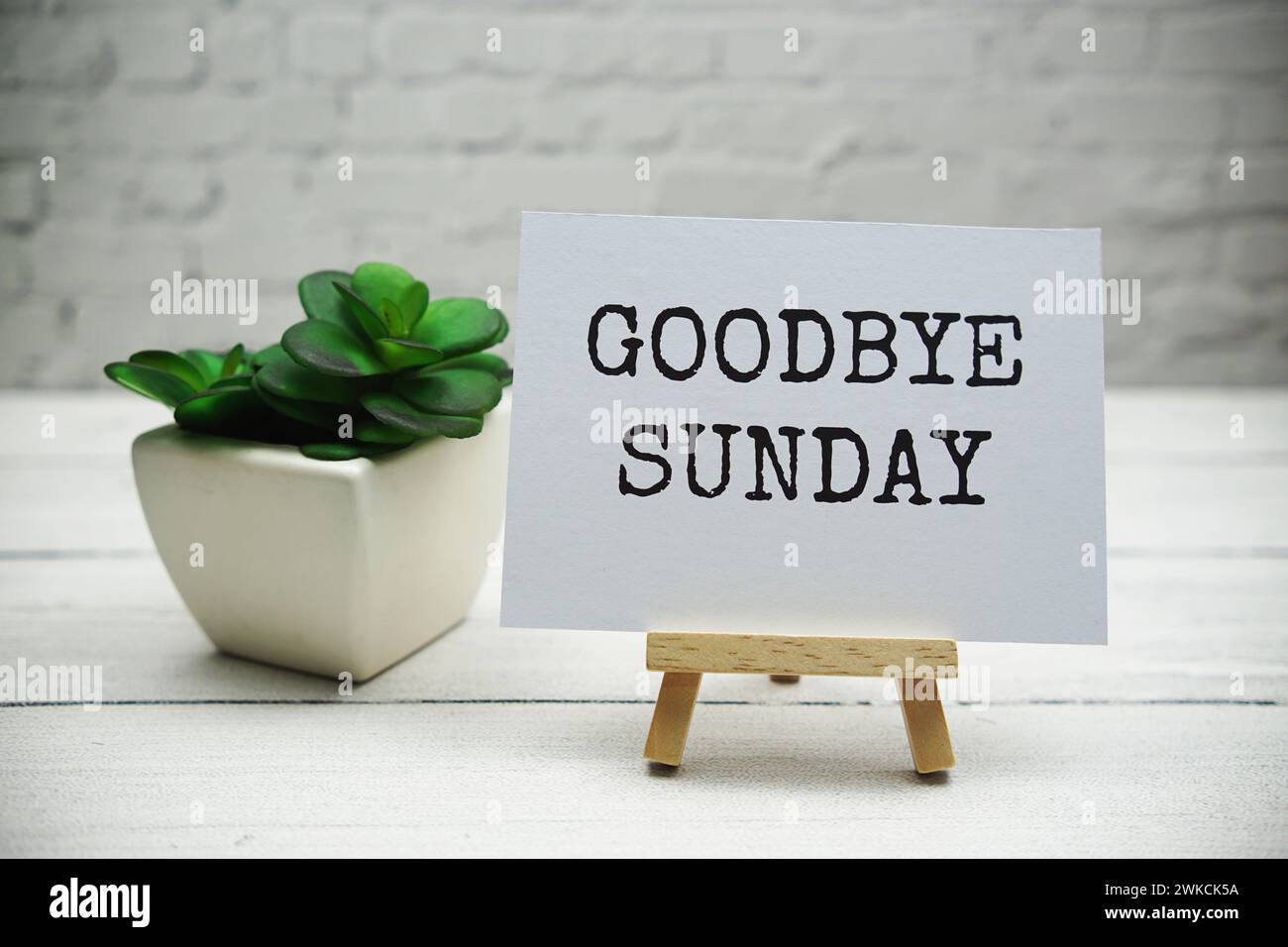 Goodbye Sunday text on wooden easel standing on white brick wall and ...