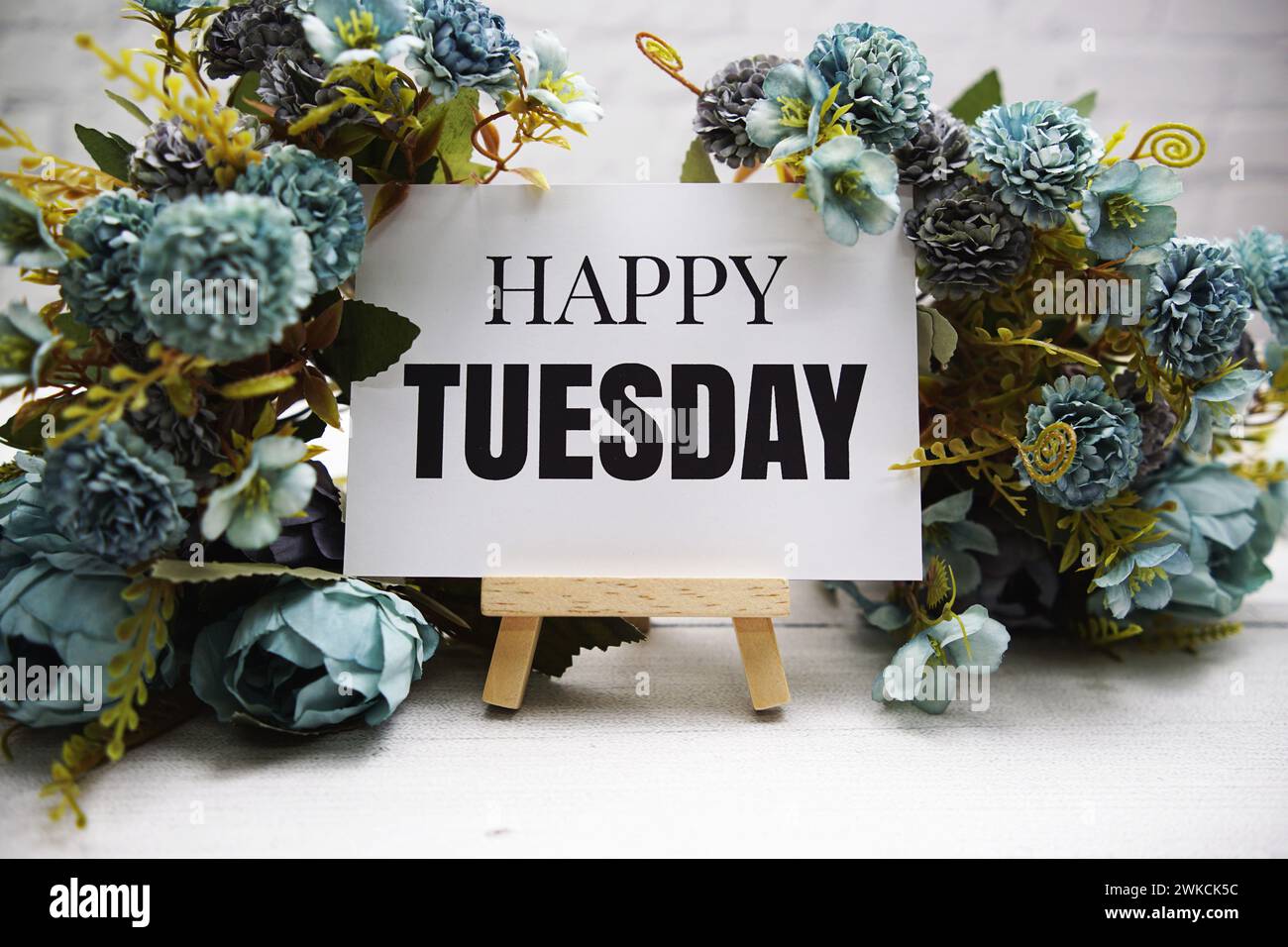 Happy Tuesday text on wooden easel standing on white brick wall and ...