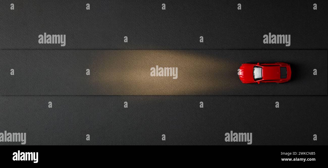 Top view of red toy car and yellow headlights on dark gray background ...
