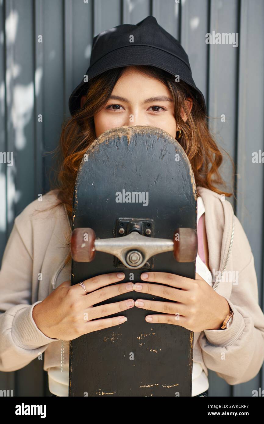 Portrait of smiling schoolgirl hiding face behind skateboard Stock ...