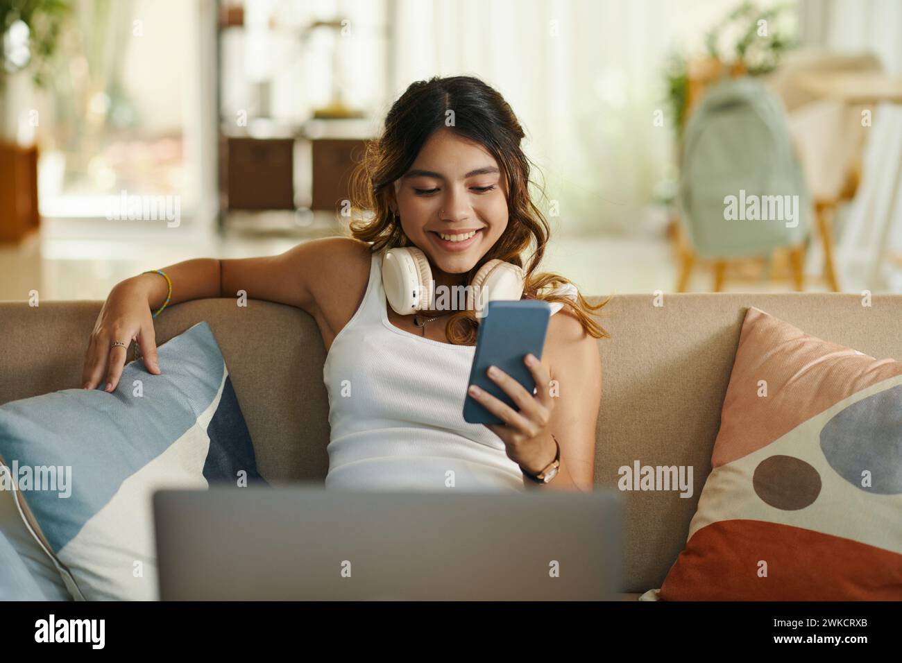 Happy girl sitting on couch and texting friends instead of studying ...