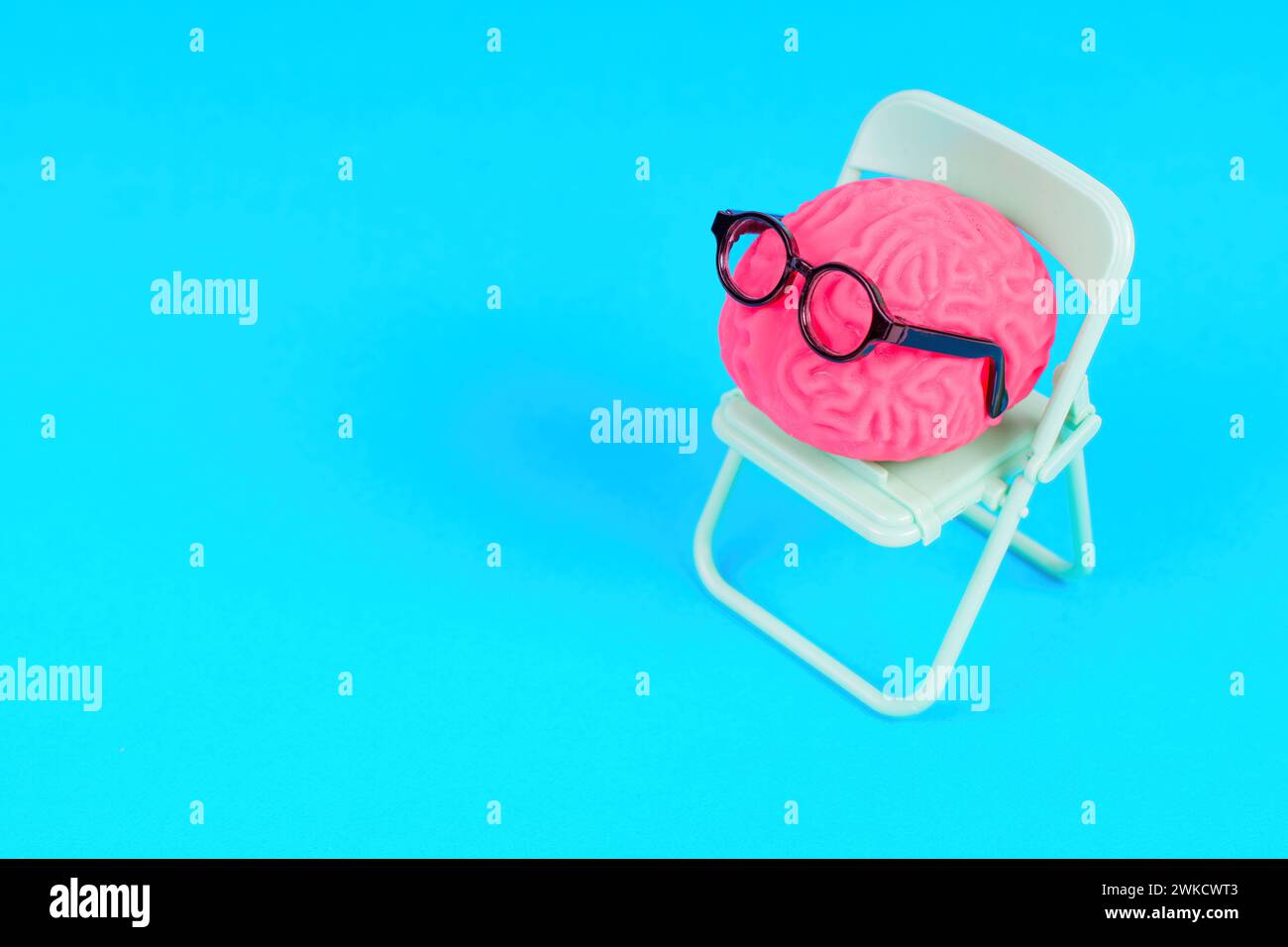 Human brain model, adorned with glasses, seated on a folding teal chair ...