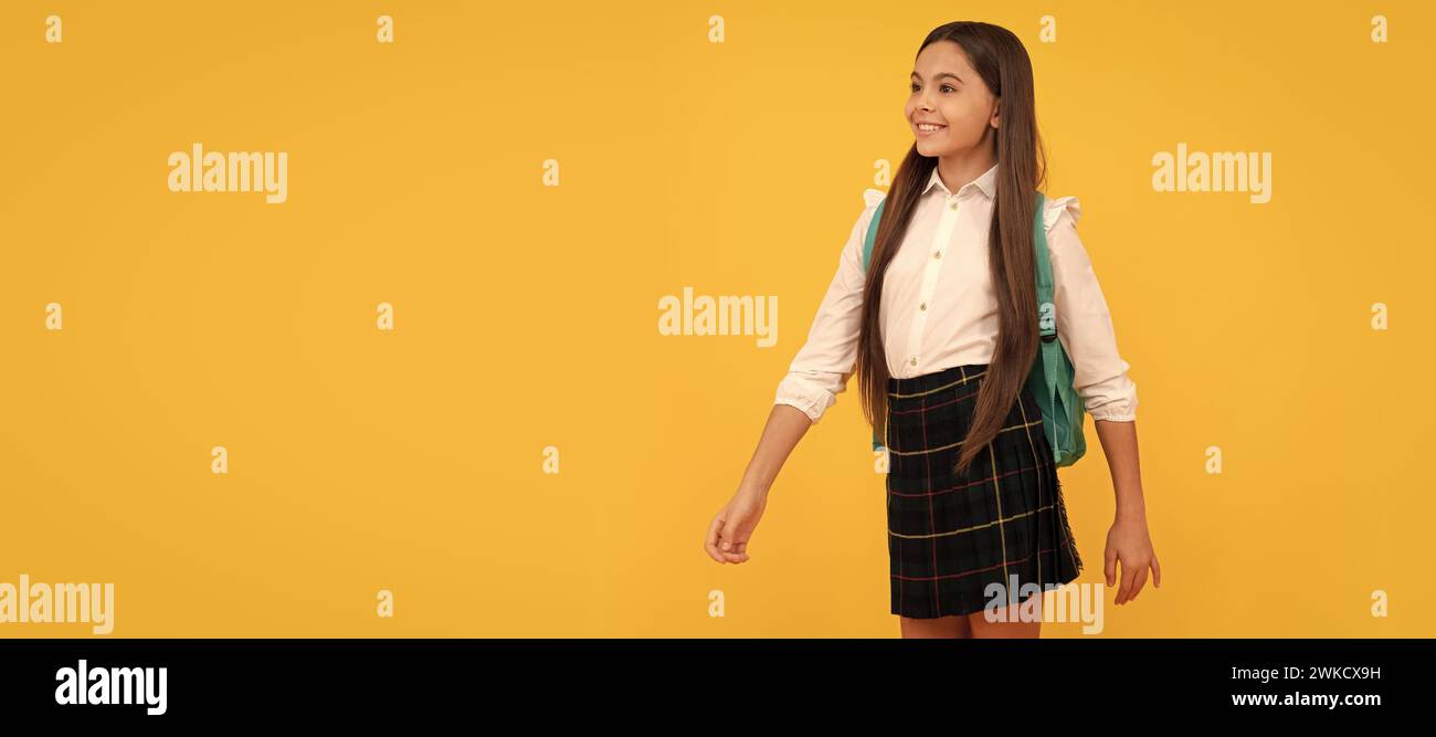 happy teen girl in school uniform full length on yellow background making step forward, school ...
