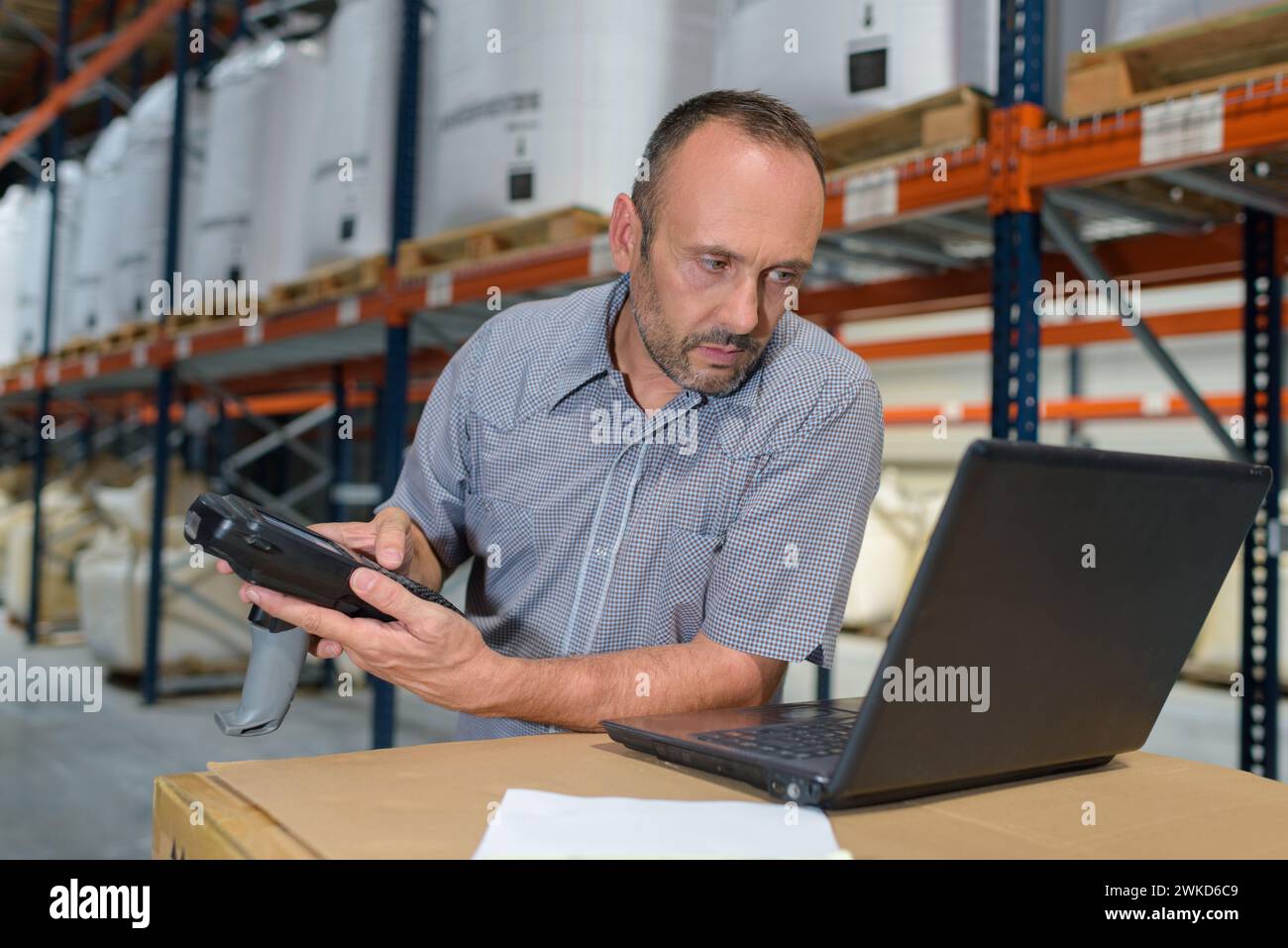 man in warehouse holding scanner and looking at laptop Stock Photo - Alamy