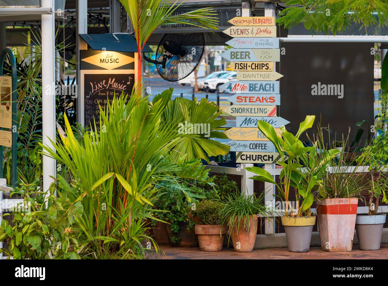 Lush tropical pot plants and a pole with multiple signs outside the ...