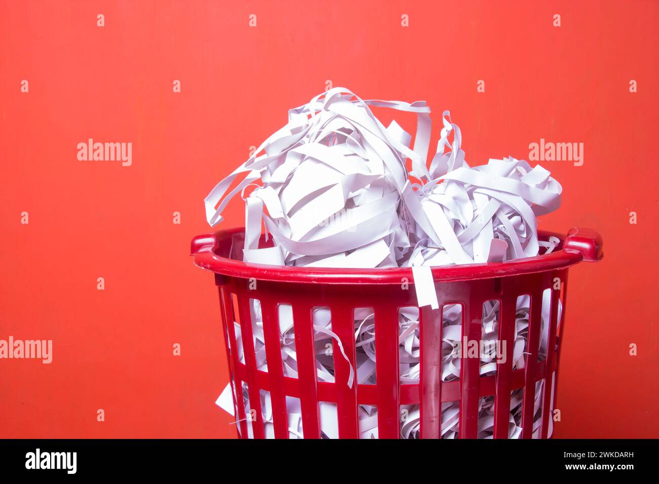 front view of red trash can full of waste paper with irregular cuts on ...
