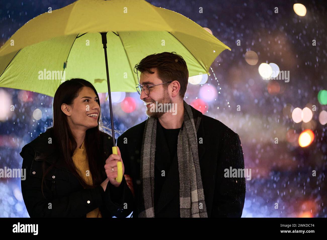 In the romantic ambiance of a rainy night, a happy couple walks through the city, sharing tender ...