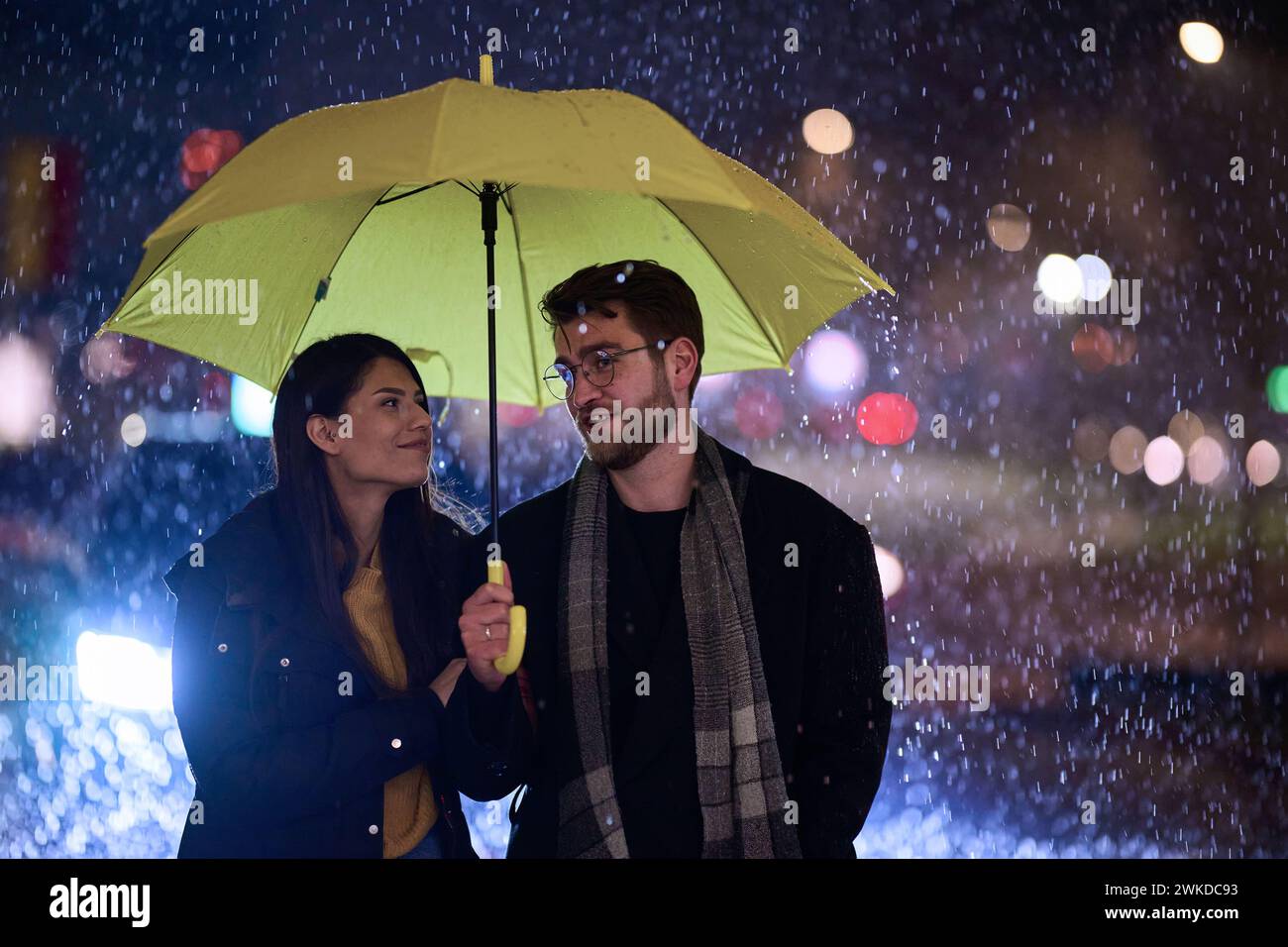 In the romantic ambiance of a rainy night, a happy couple walks through ...