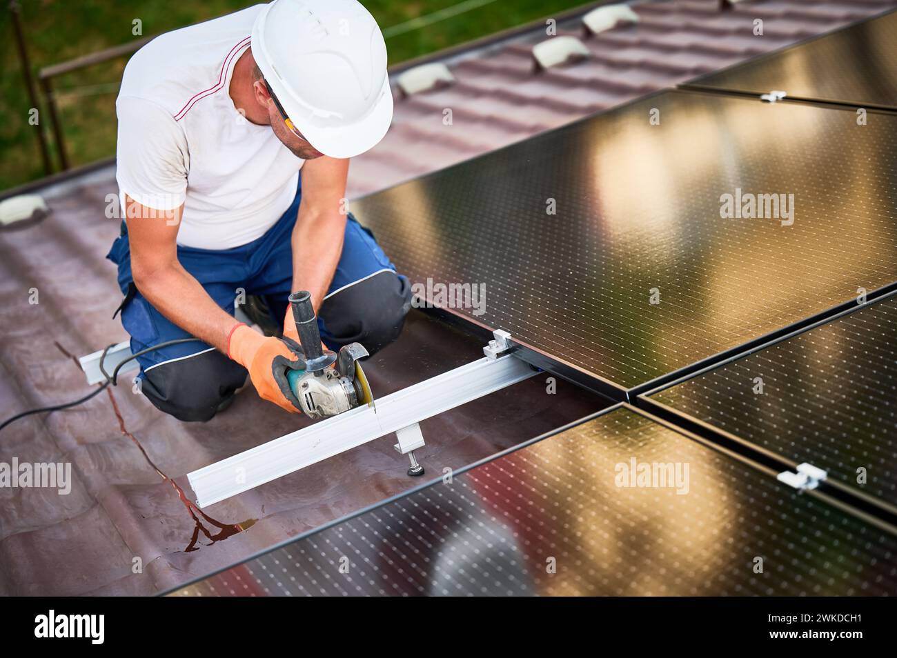 Worker installing or maintaining photovoltaic solar panel system on roof of house. Technician in ...