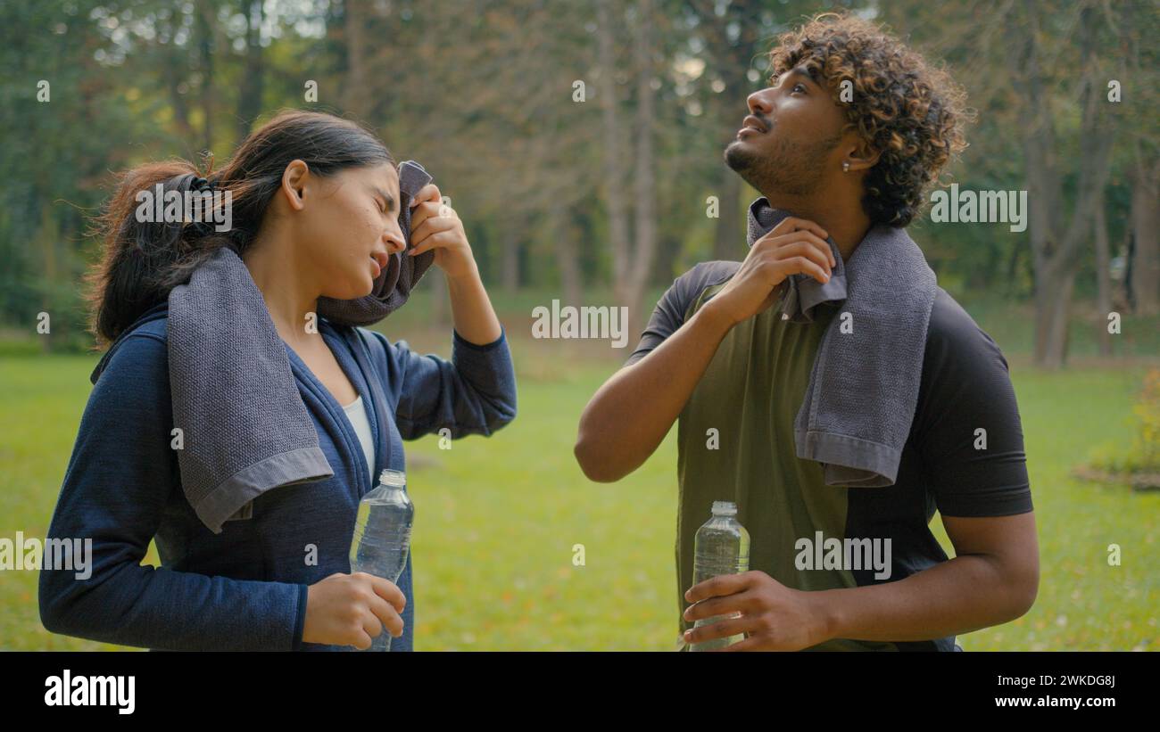 Tired exhausted Indian man and woman relaxing after sports in park ...