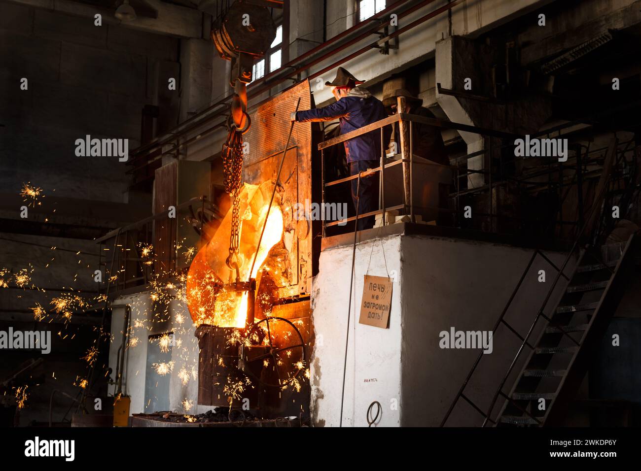 Worker manages molten metal pouring in industrial environment, steel ...