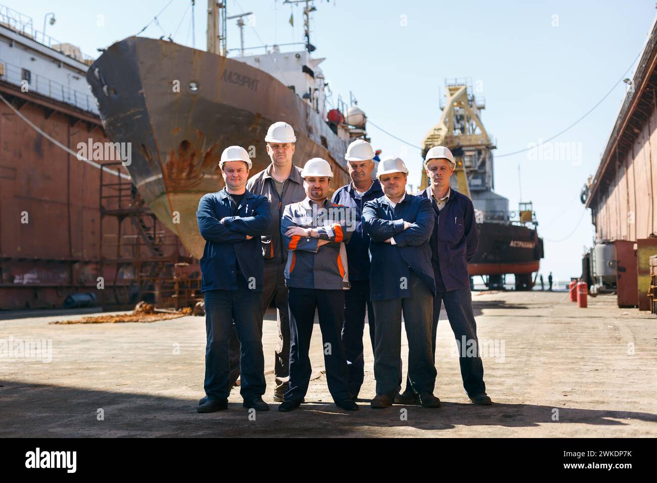 Team of shipyard workers stand proudly at dry dock. Marine engineers in ...