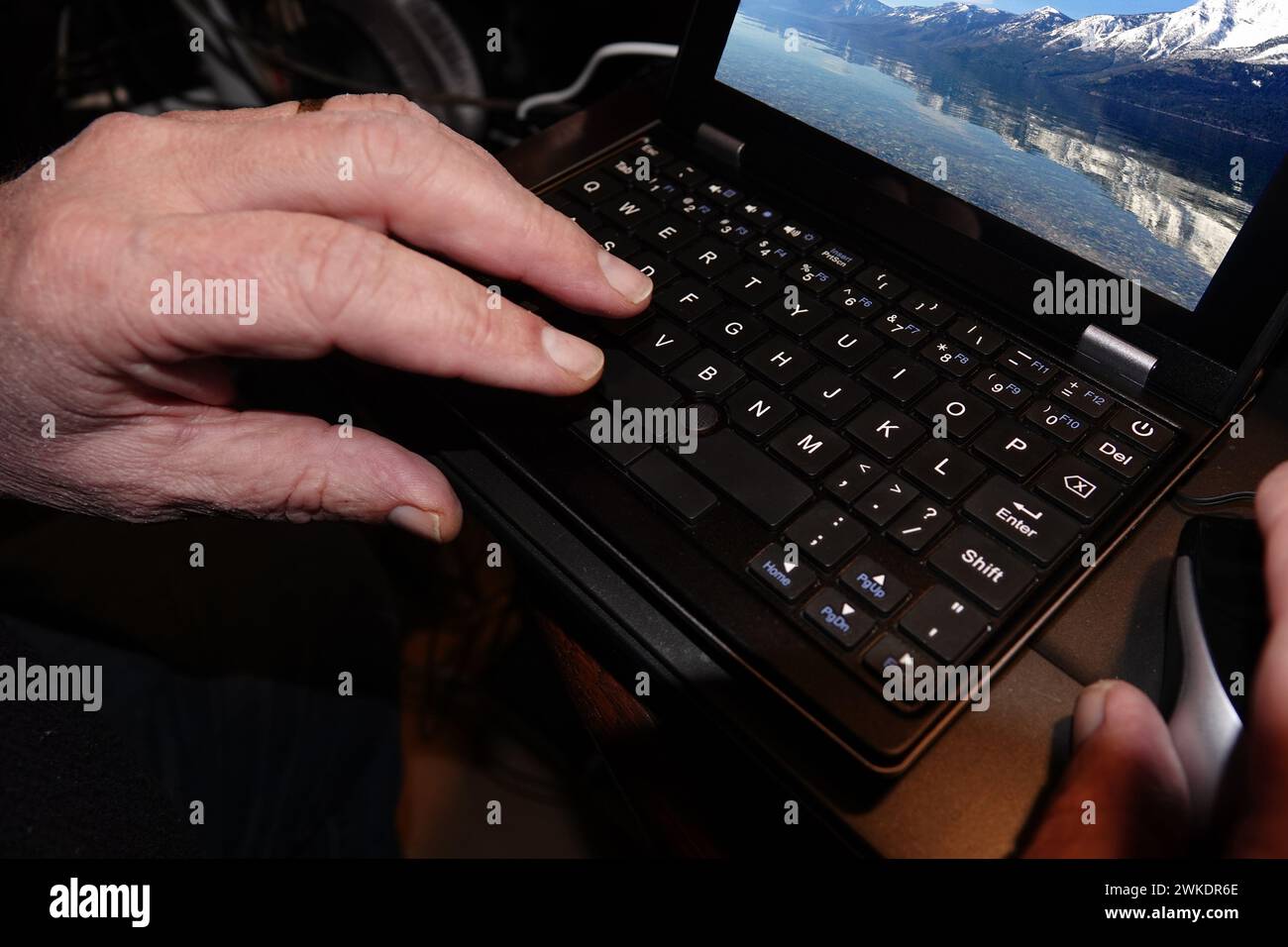 A modern 7 inch mini pocket laptop with the hand of an older man. An ...