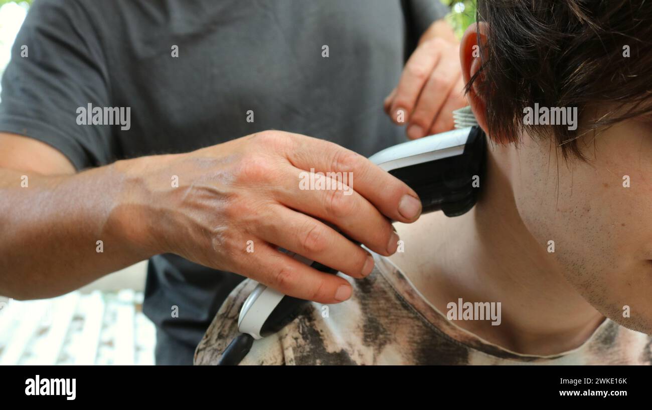 A man trims a machine for a teenager with long dark hair on the street ...