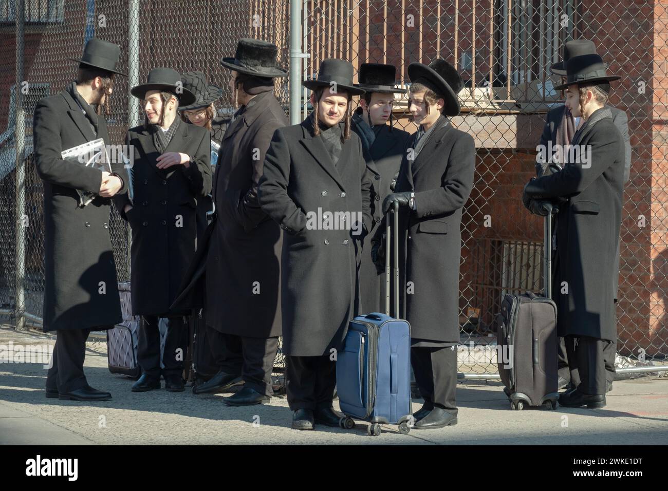 A group of orthodox Jewish young men, some with suitcases, wait for a ...