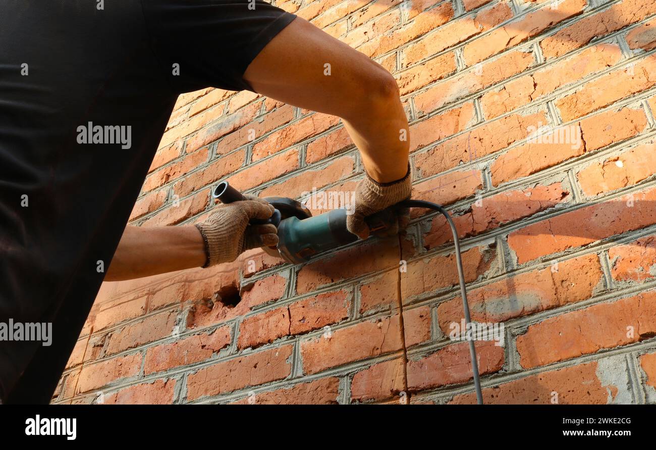 cutting the outline of a window in a brick wall with a grinder, a man ...