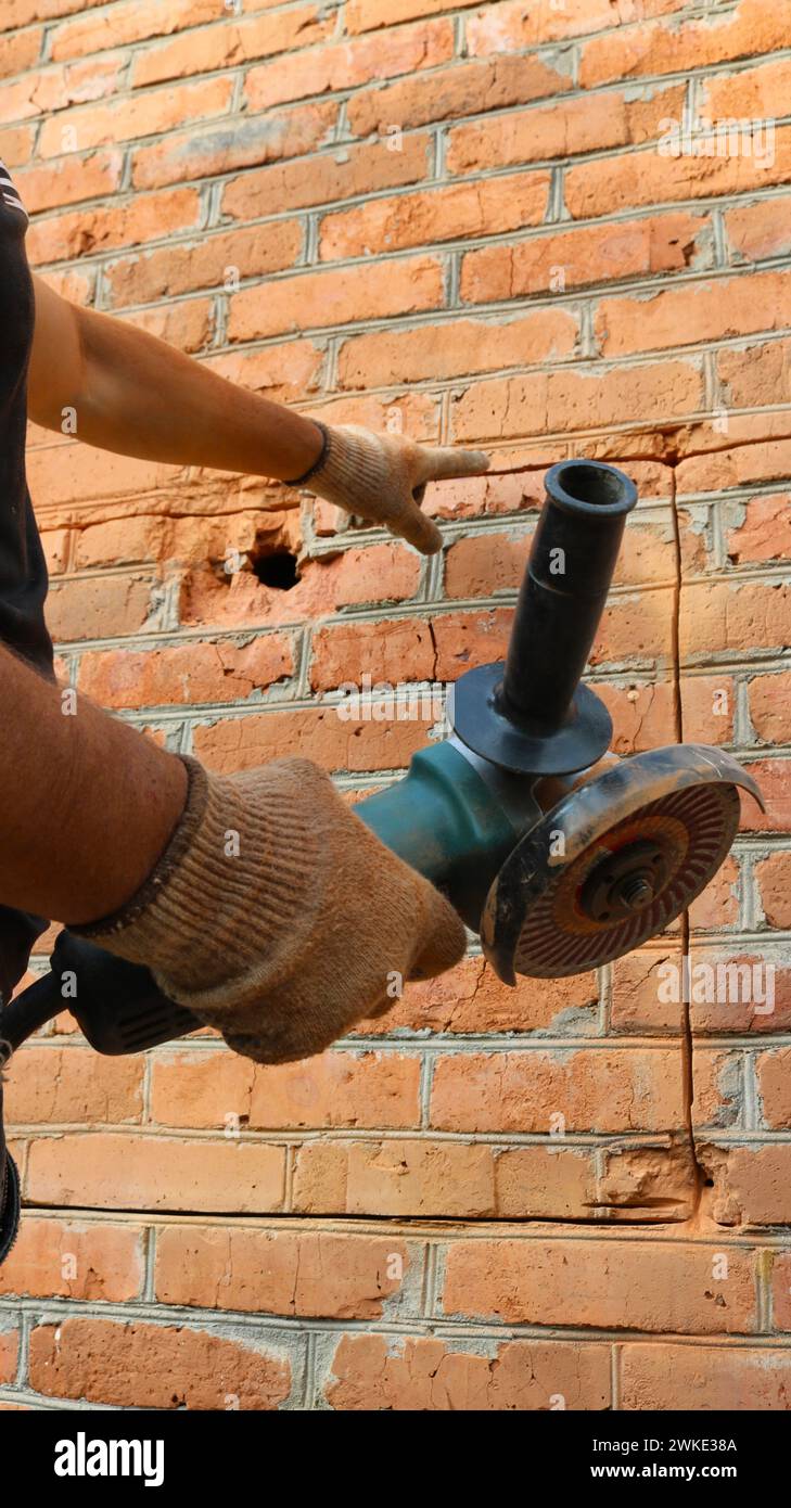 a builder in gloves with an angle saw stands near a red brick wall and ...