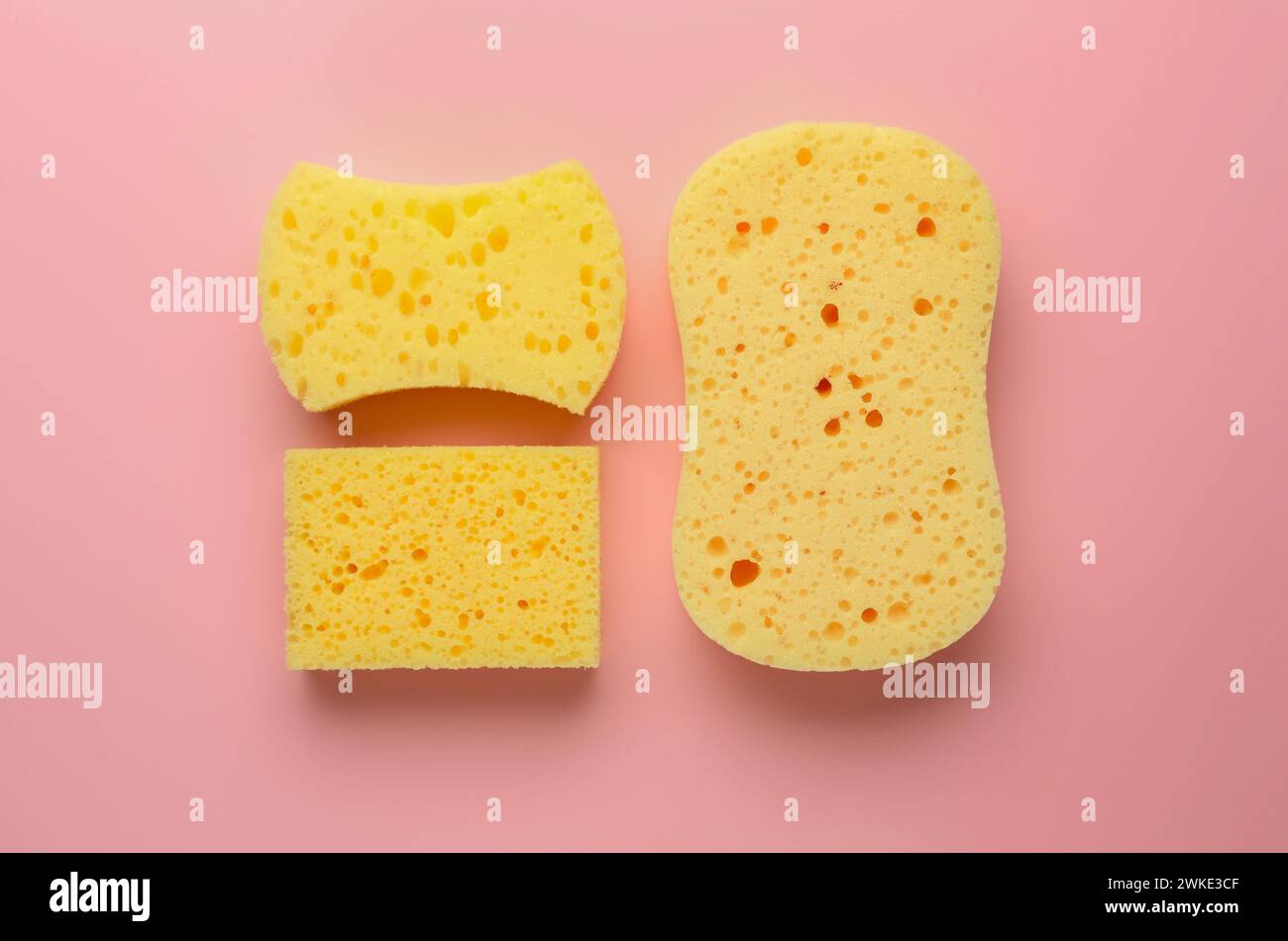 New yellow sponges of different shapes on pink background, flat lay ...