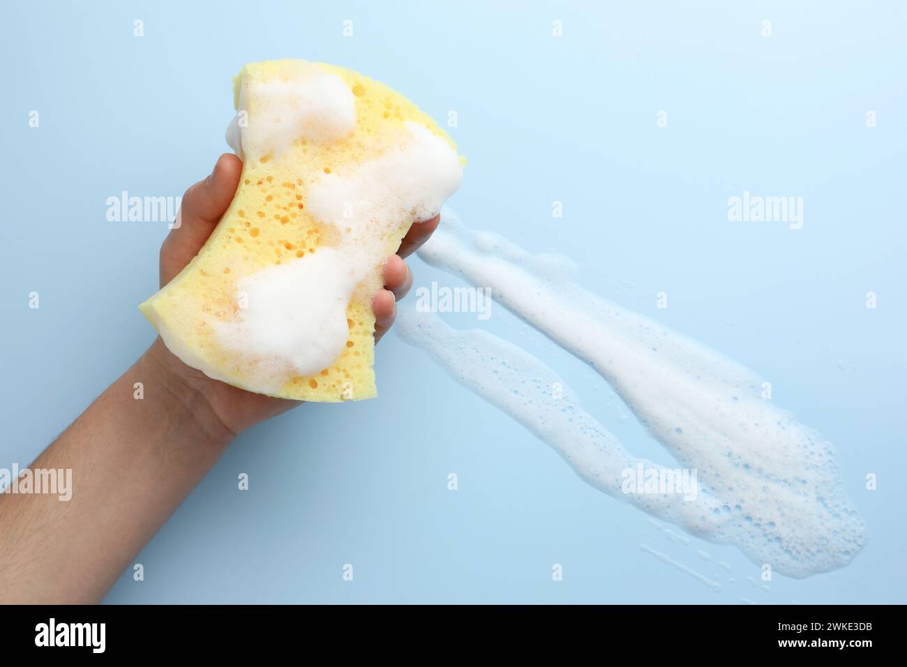 Man holding sponge with foam on light blue background, top view Stock ...