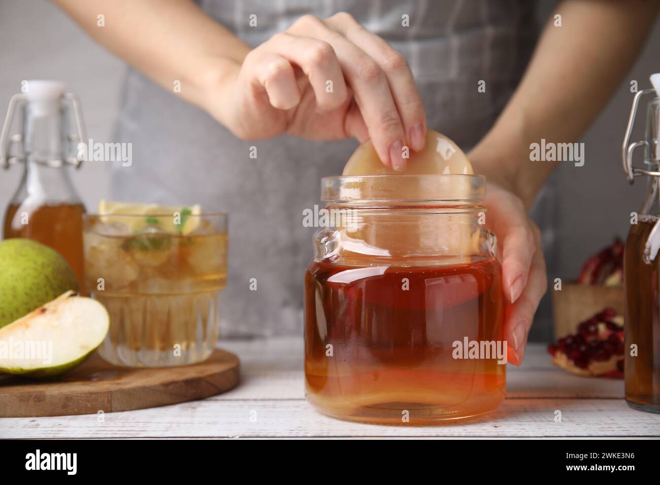 Woman putting Scoby fungus into jar with kombucha at white wooden table ...