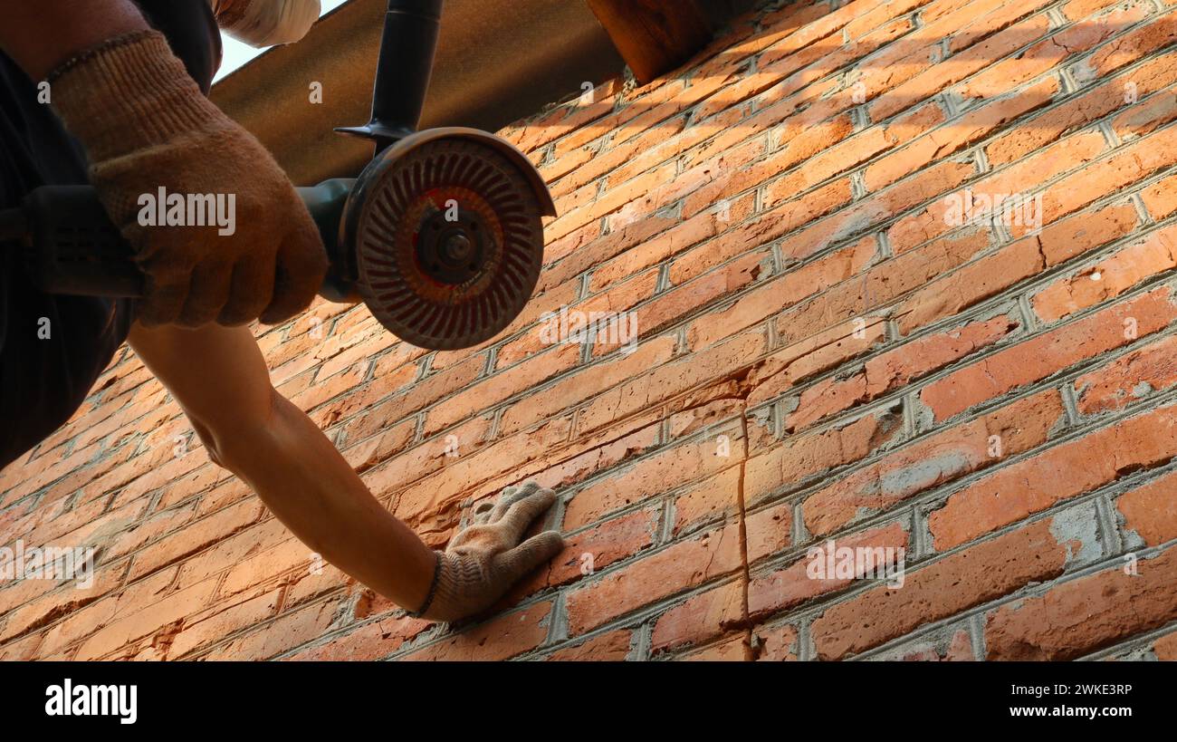 a builder with a grinder and a stone cutting disc stands by a brick ...