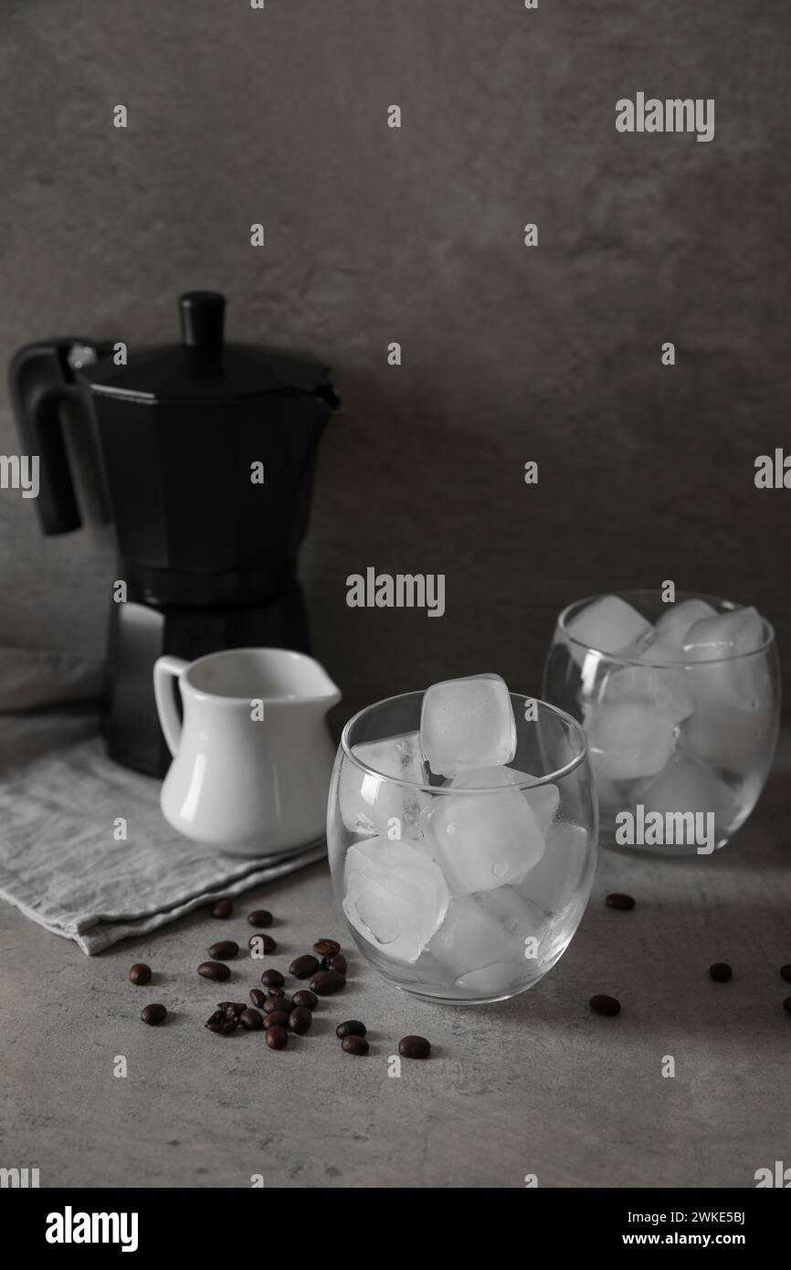 Making iced coffee. Ice cubes in glasses and ingredients on gray table ...