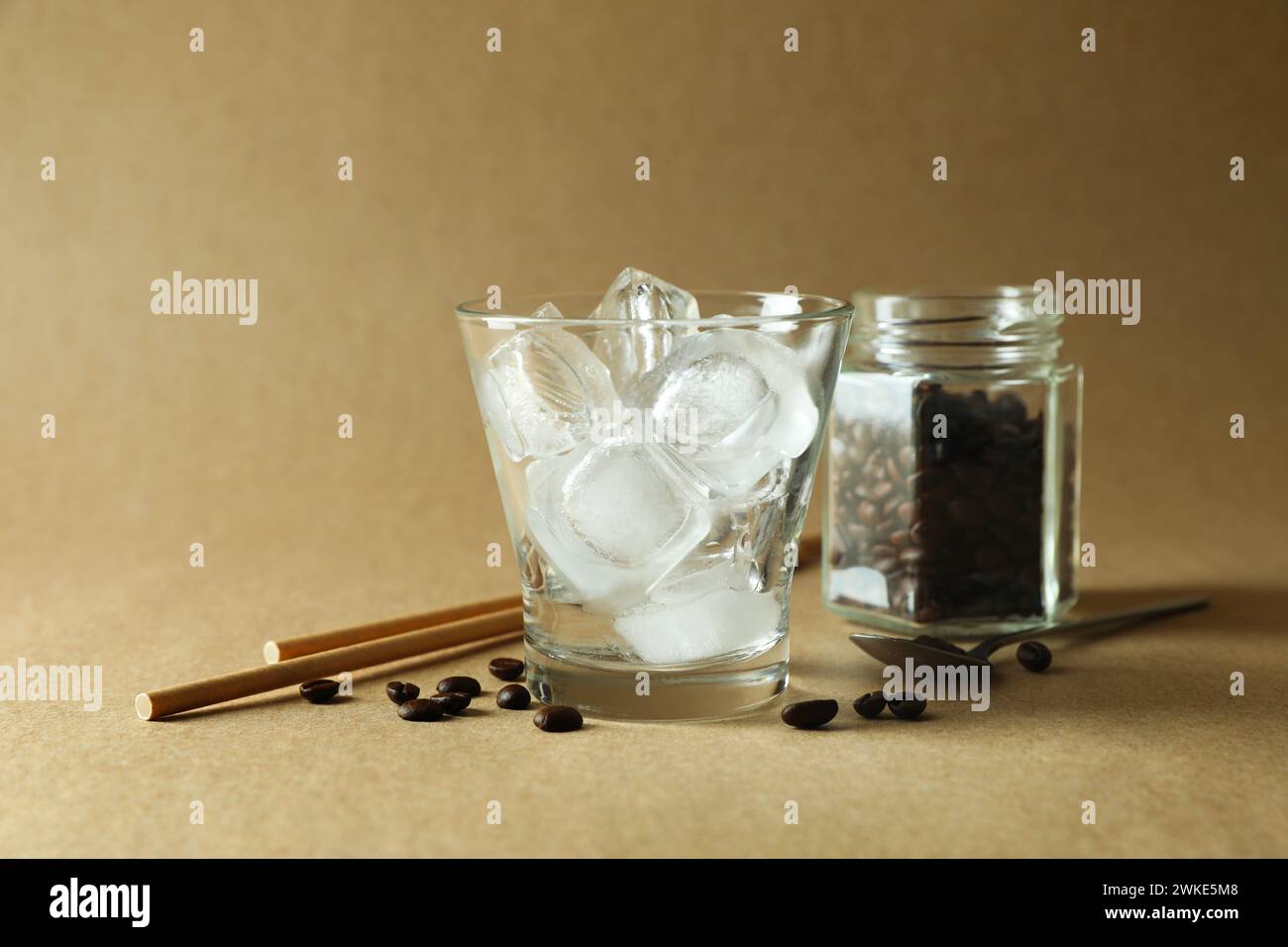 Cooking iced coffee. Ice cubes in glass, beans and straws on beige ...