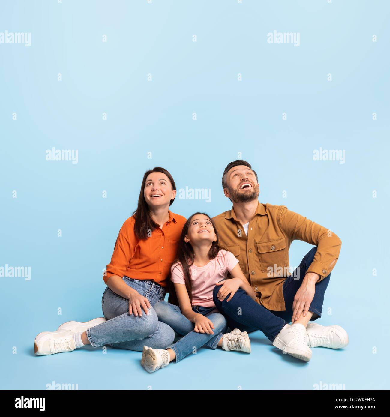 Joyful family of three looking up sitting on blue background Stock ...