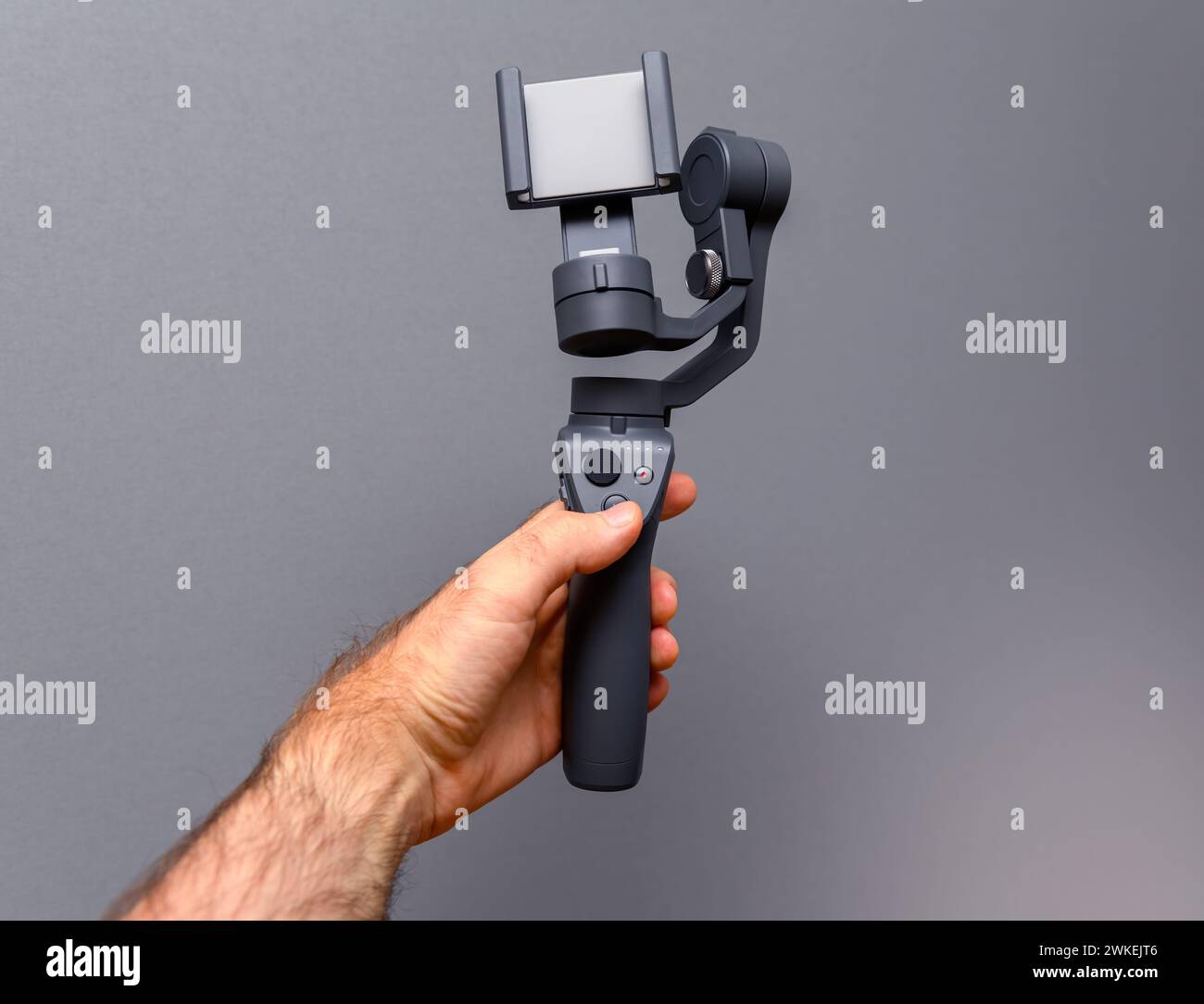 A male hand firmly grips a camera stabilizer against a neutral gray ...