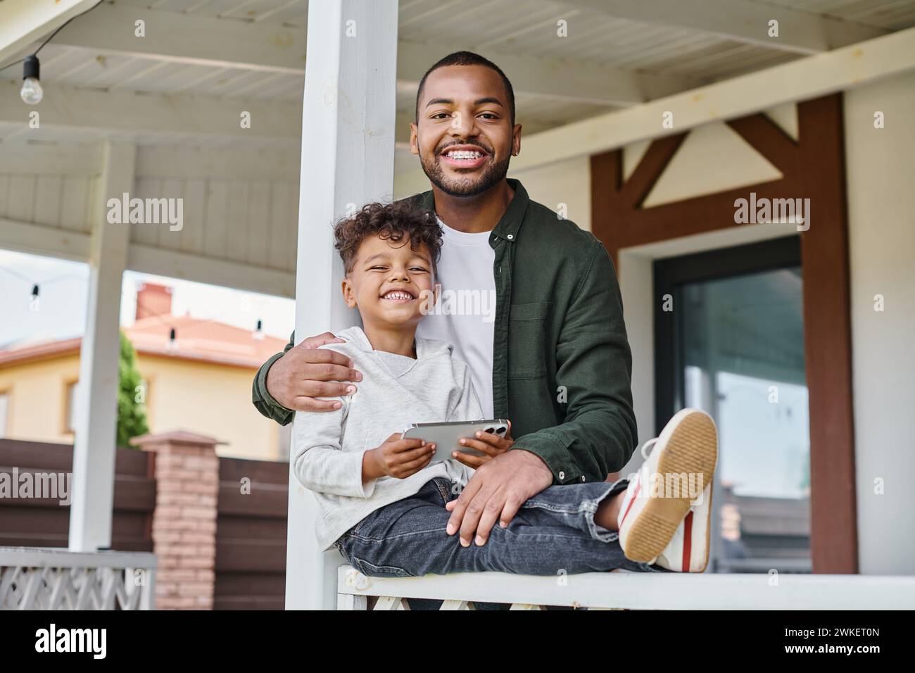 joyful african american father hugging son sitting on porch and holding ...