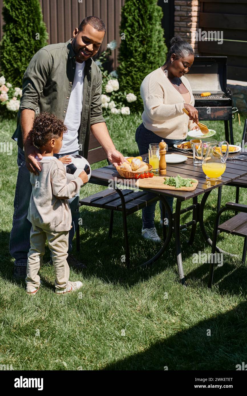 cheerful african american parents serving table in garden near son ...
