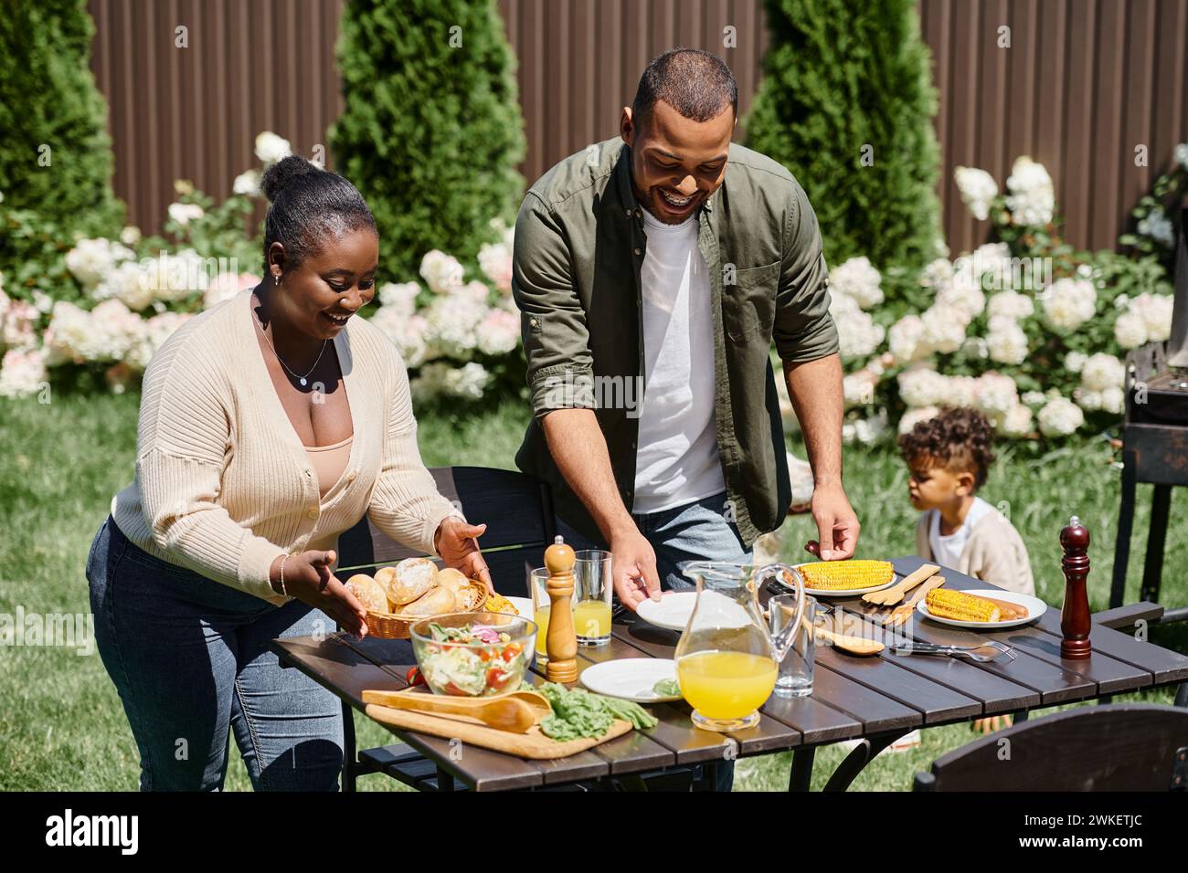 cheerful african american parents serving table in garden near son ...
