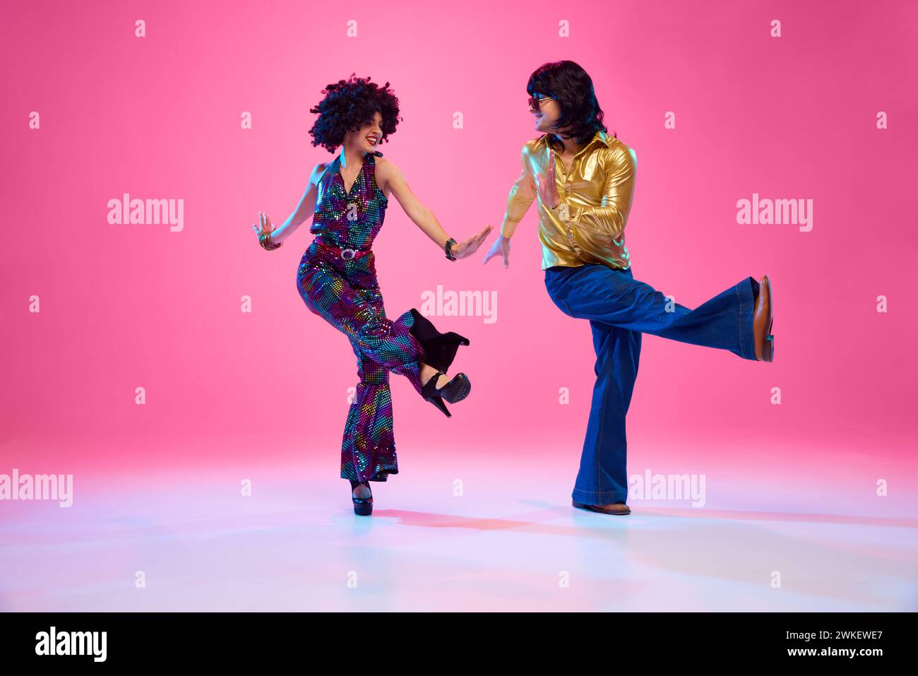 Man and woman dressed in vibrant 1970s attire dancing in motion against ...